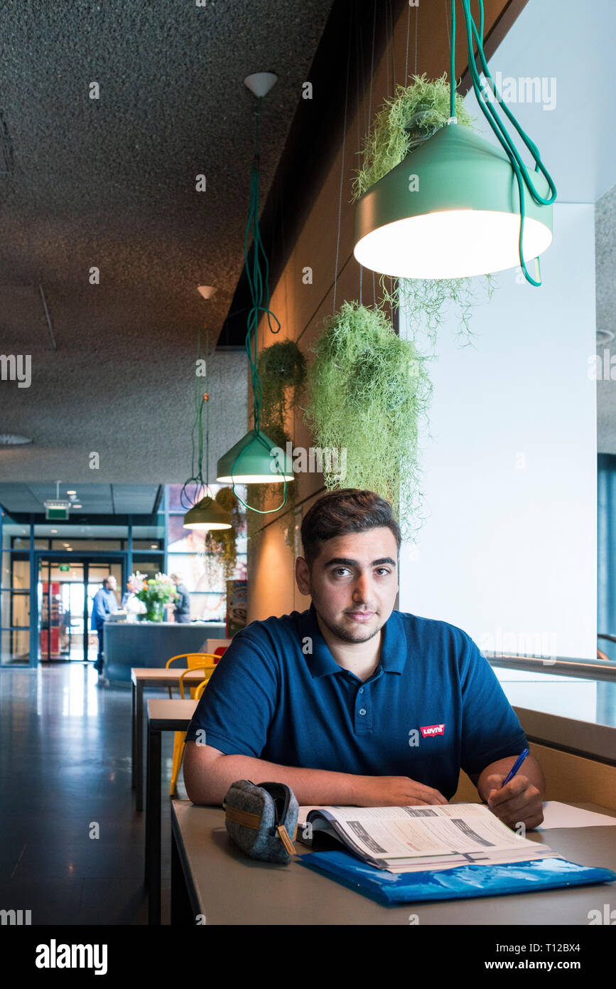 A young arabic male student sits at a table studying with his books ...