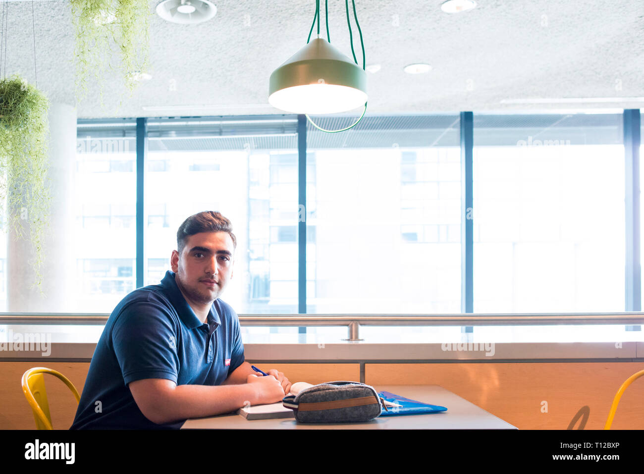A young arabic male student sits at a table studying with his books ...
