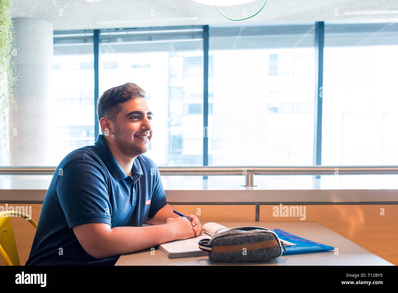 A young arabic male student sits at a table studying with his books ...