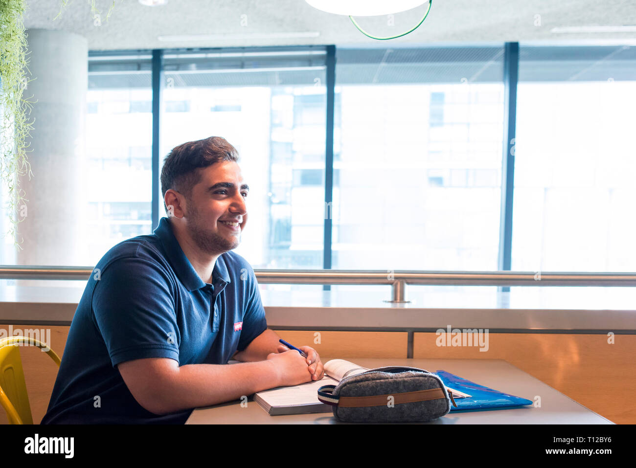 A young arabic male student sits at a table studying with his books ...