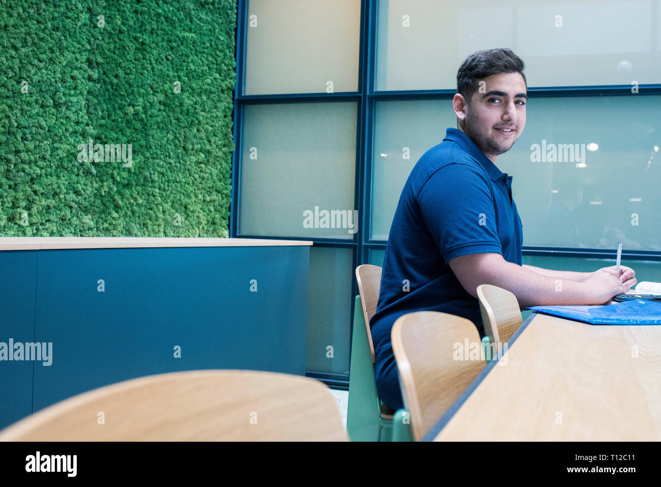 A young arabic male student sits at a table studying with his books ...