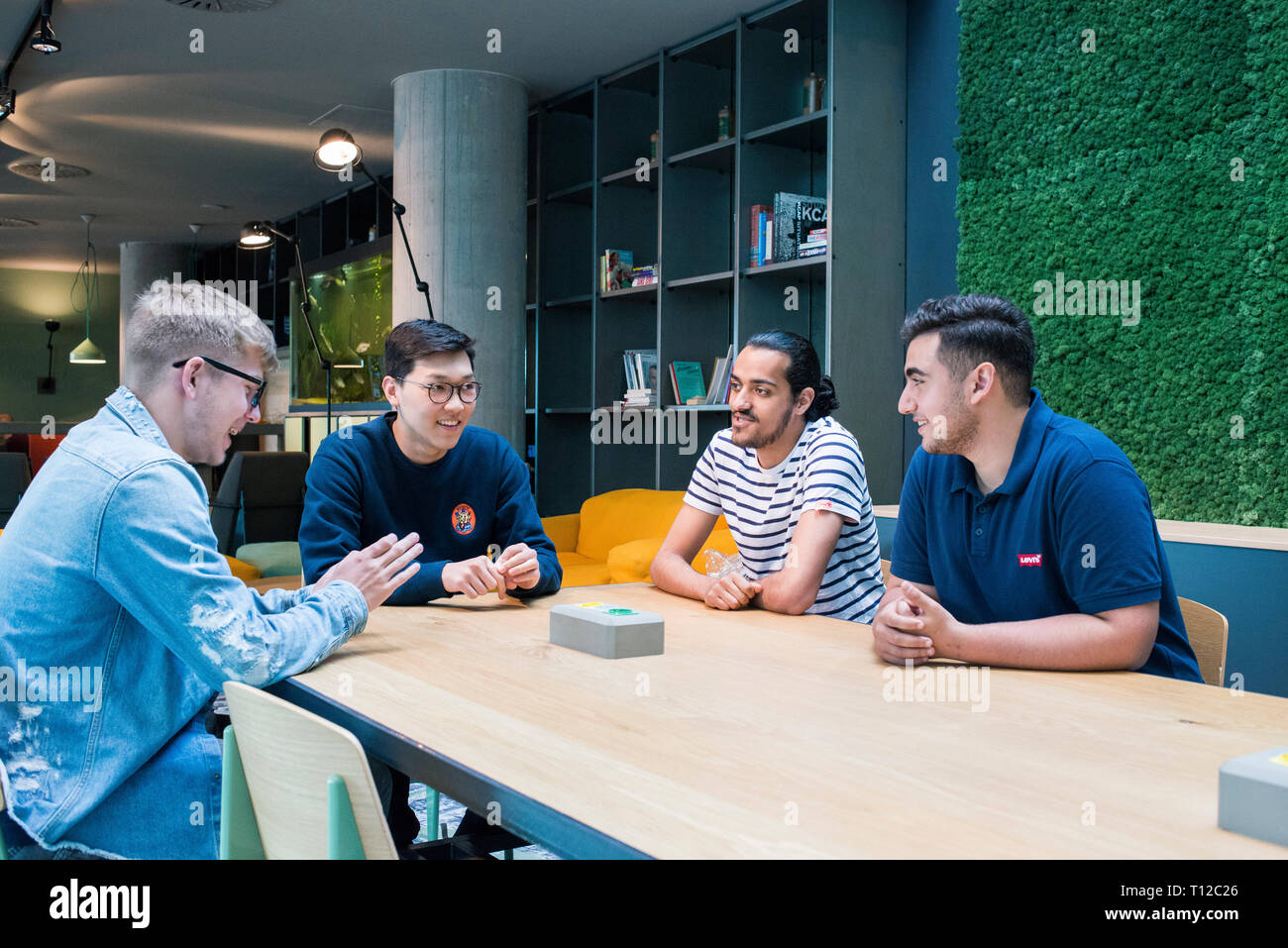 A group of young people sitting around a table chatting with each other ...