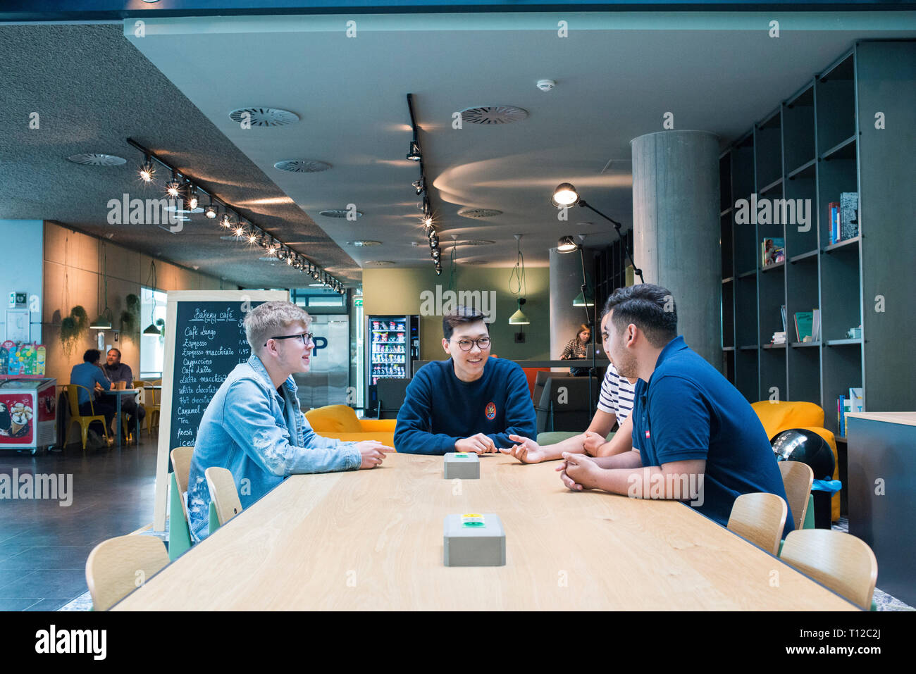 A group of young people sitting around a table chatting with each other ...