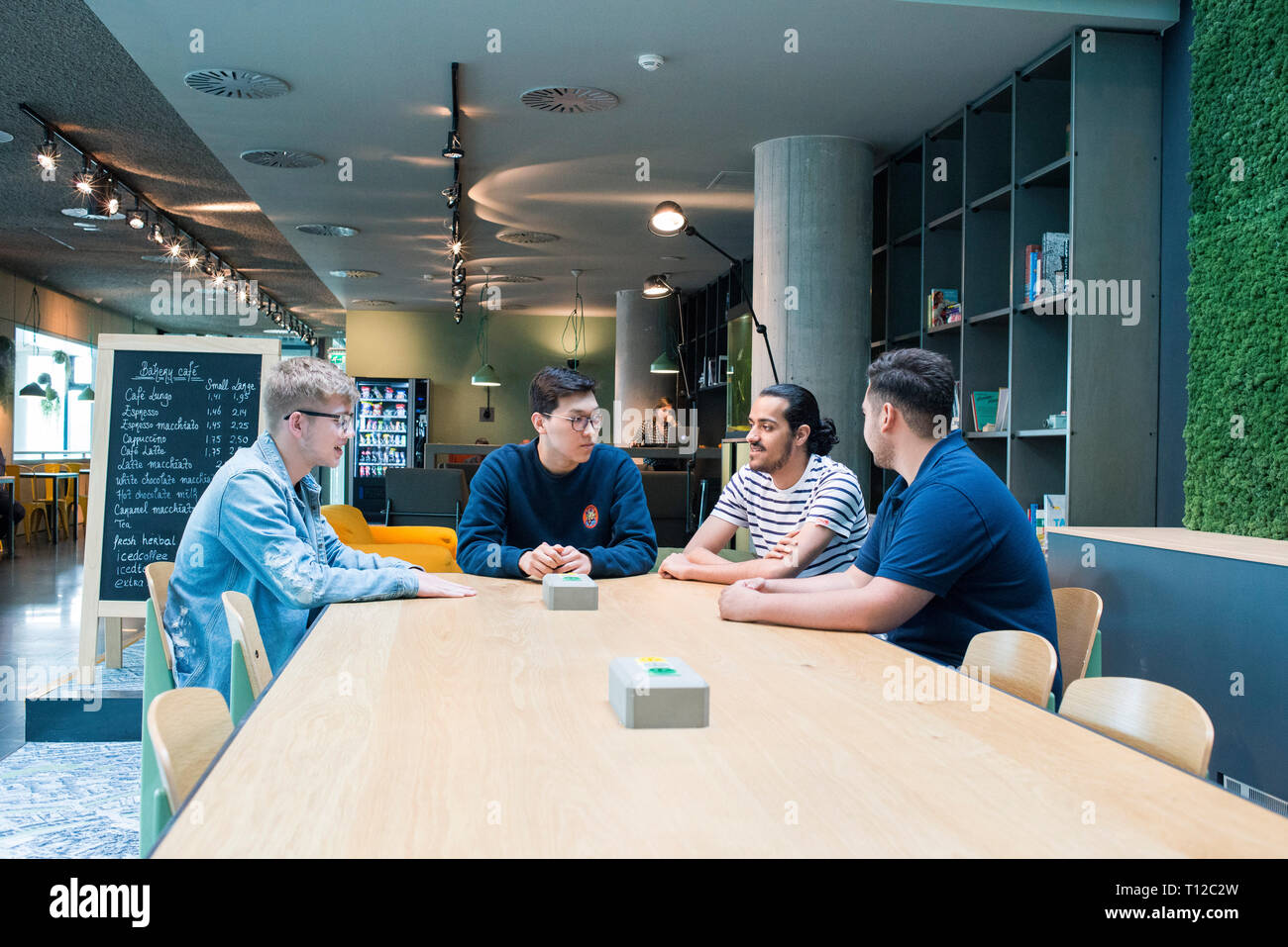 A group of young people sitting around a table chatting with each other ...