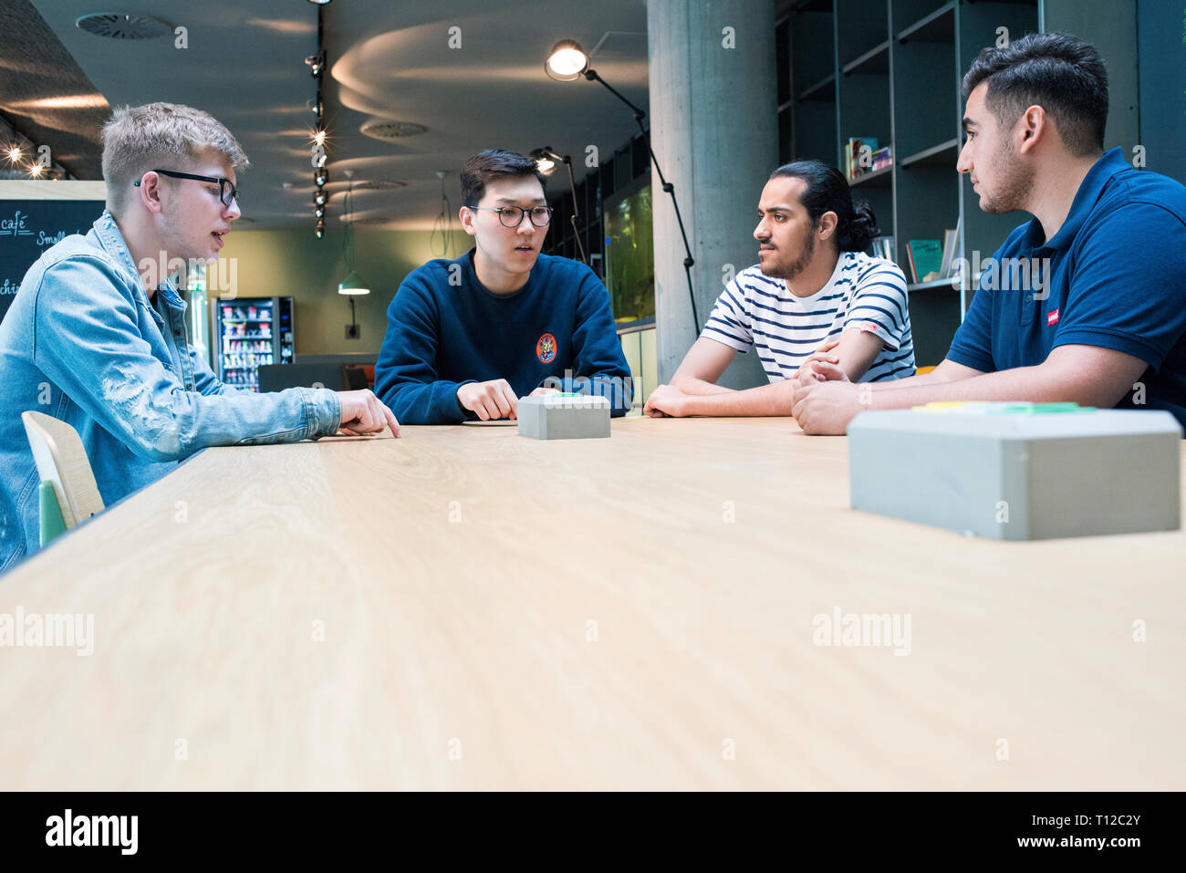 A group of young people sitting around a table chatting with each other ...