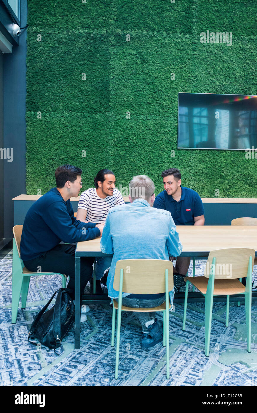 A group of young people sitting around a table chatting with each other ...