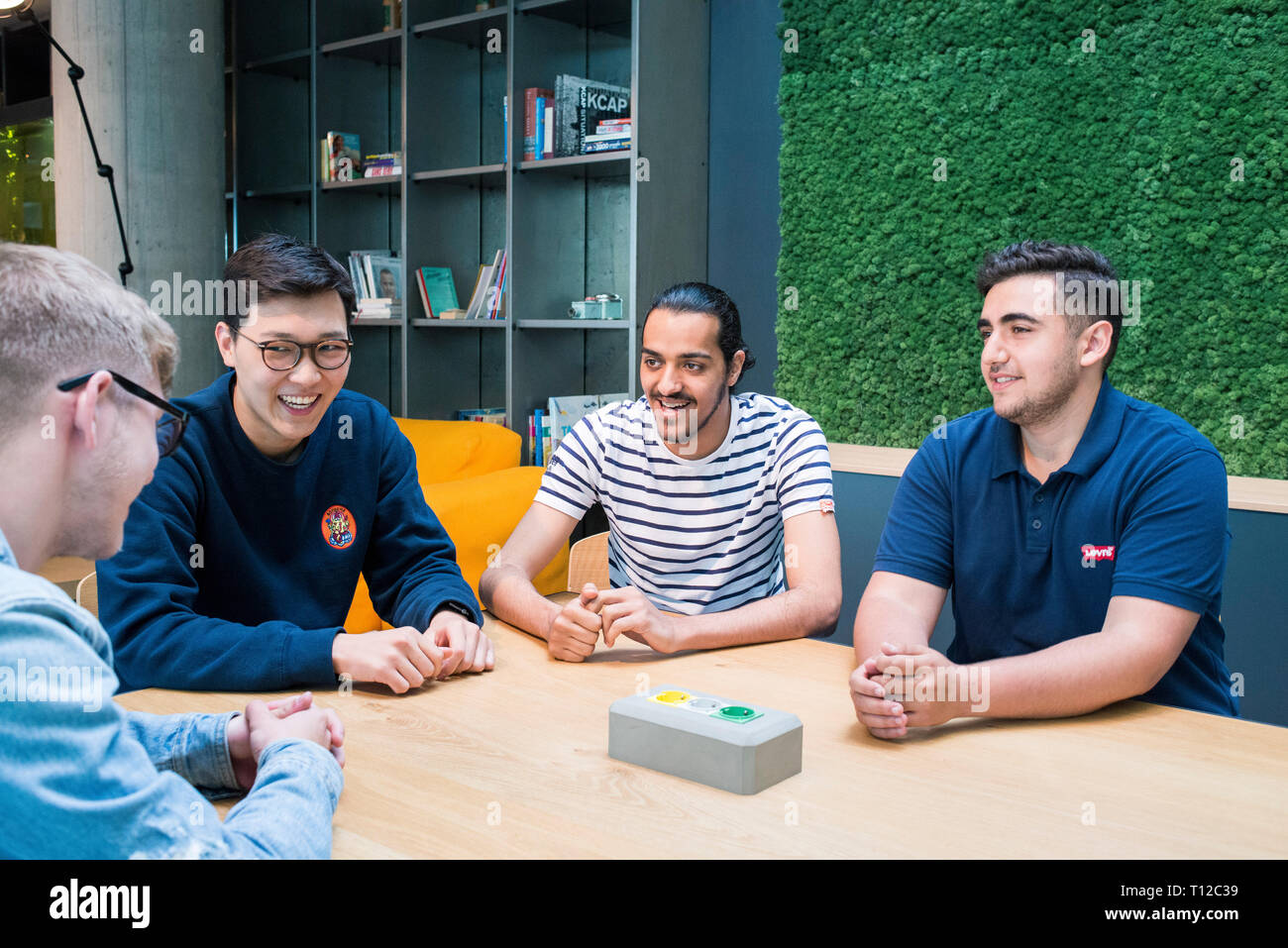 A group of young people sitting around a table chatting with each other ...