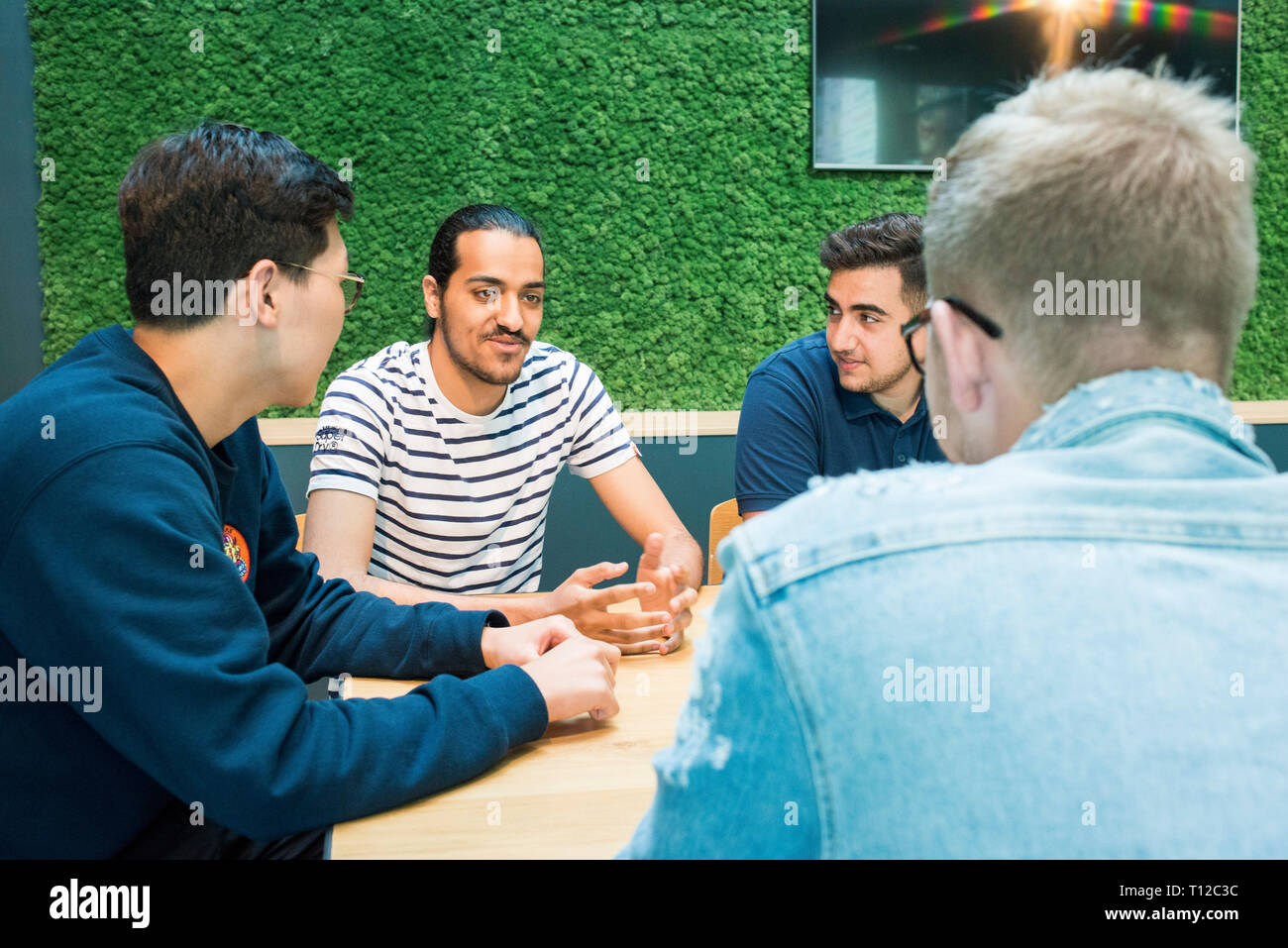 A group of young people sitting around a table chatting with each other ...