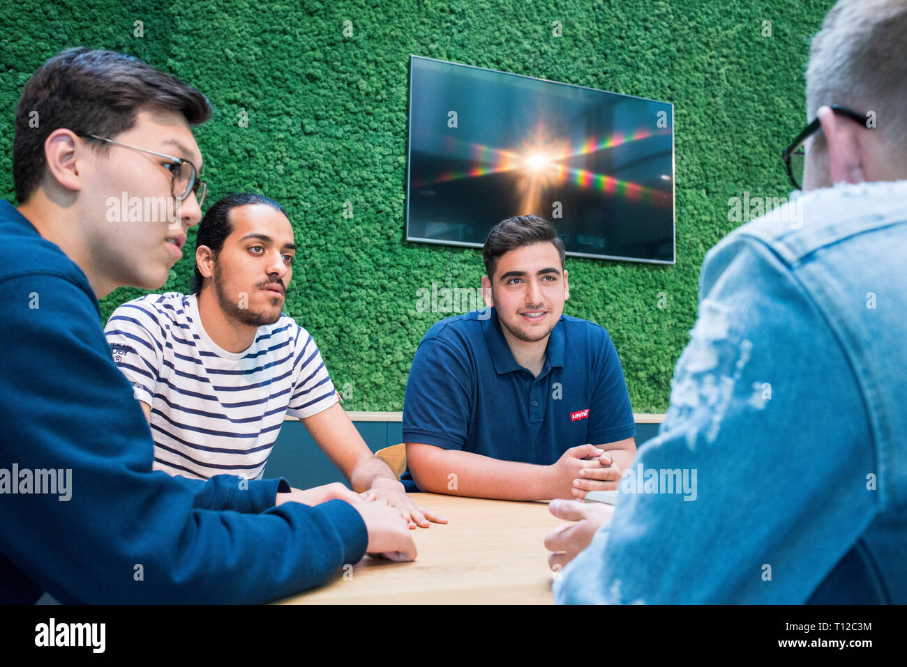 A group of young people sitting around a table chatting with each other ...