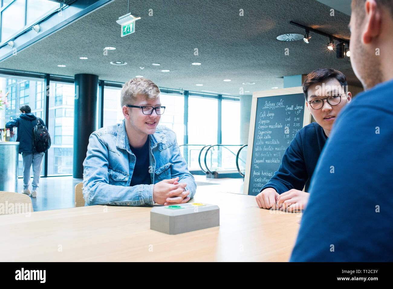 A group of young people sitting around a table chatting with each other ...