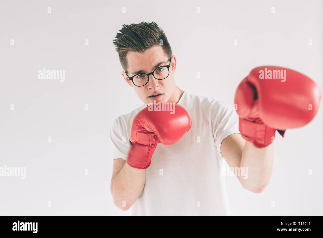 Cowardly funny young man in red boxing gloves. Nerd is wearing glasses ...