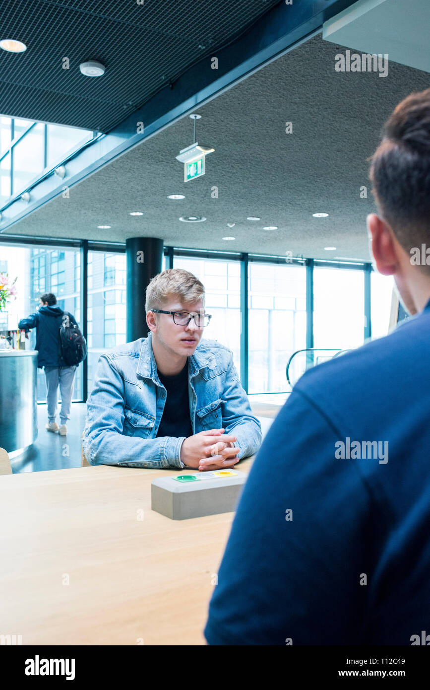 A group of young people sitting around a table chatting with each other ...