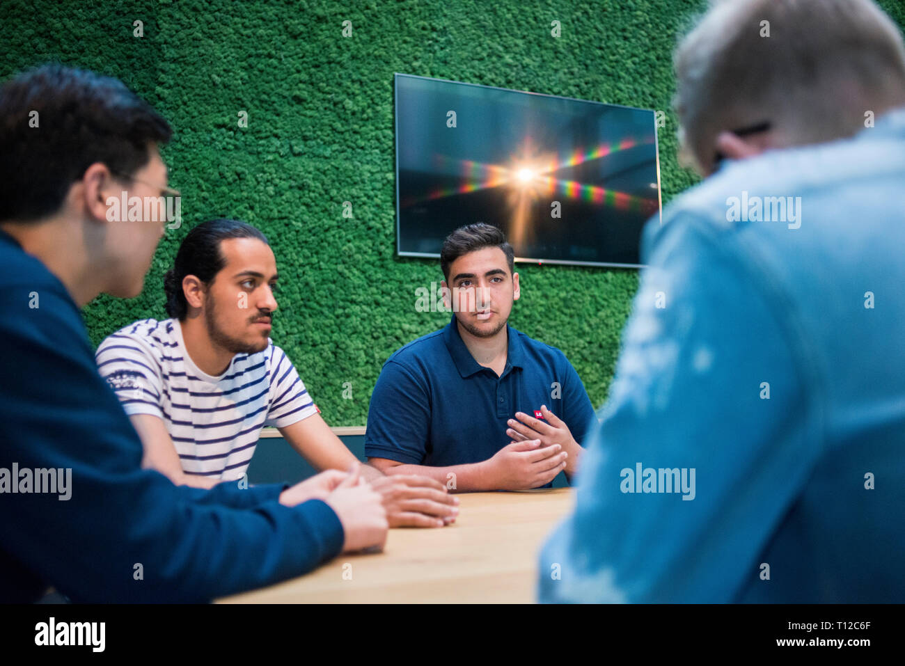 A group of young people sitting around a table chatting with each other ...