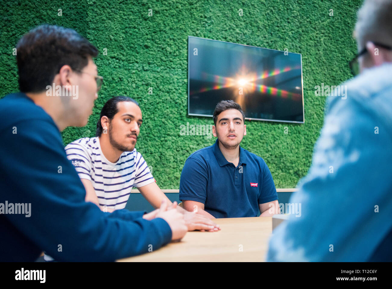 A group of young people sitting around a table chatting with each other ...