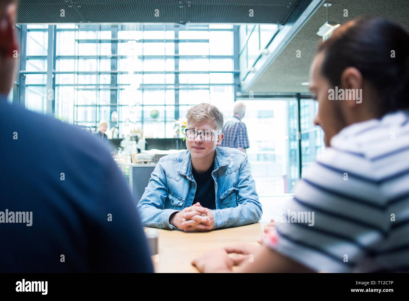A group of young people sitting around a table chatting with each other ...