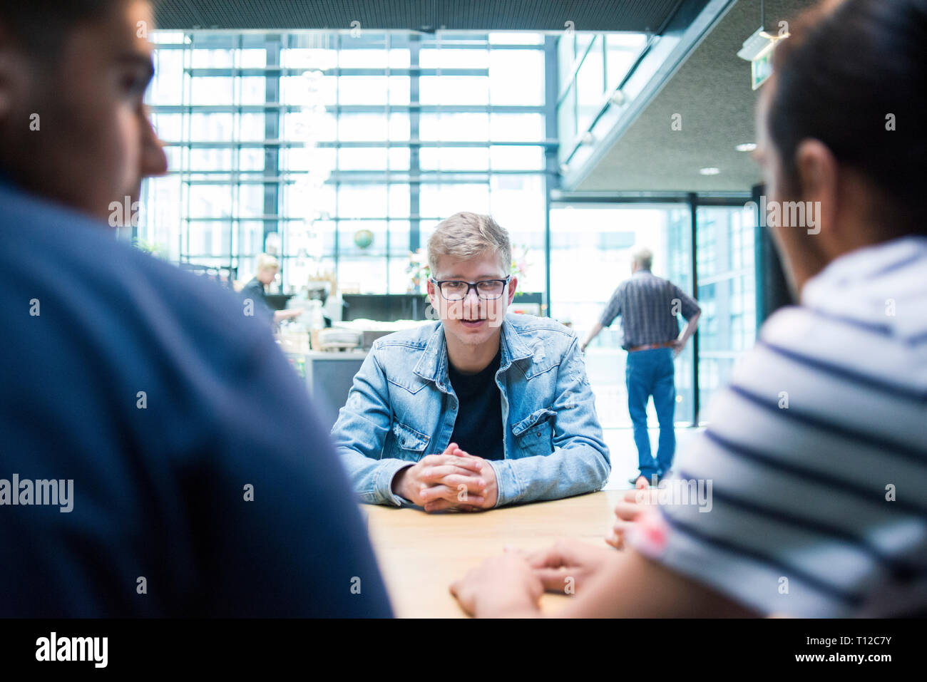 A group of young people sitting around a table chatting with each other ...