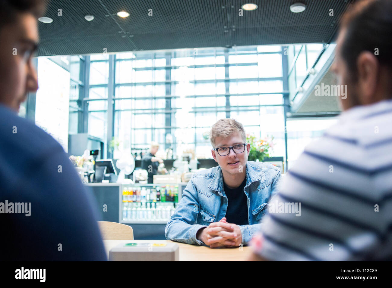 A group of young people sitting around a table chatting with each other ...