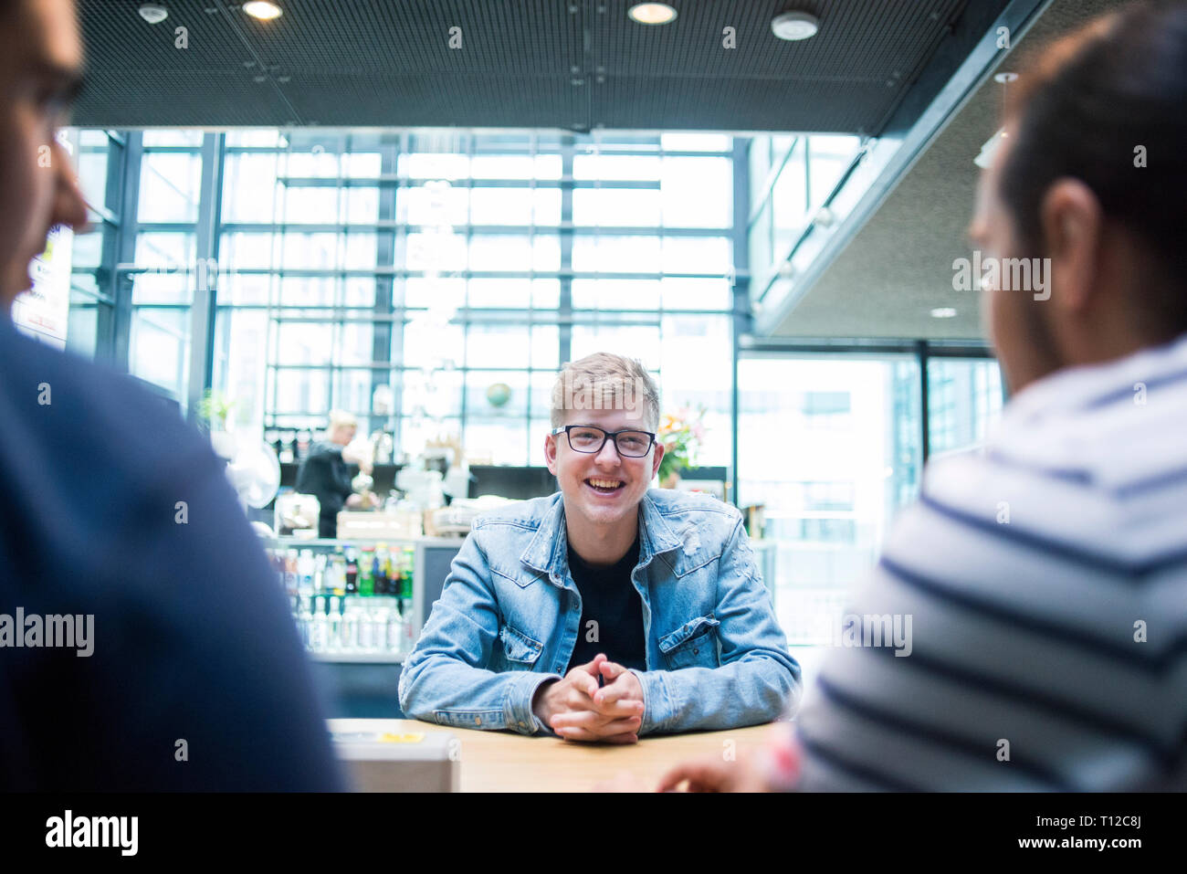 A group of young people sitting around a table chatting with each other ...