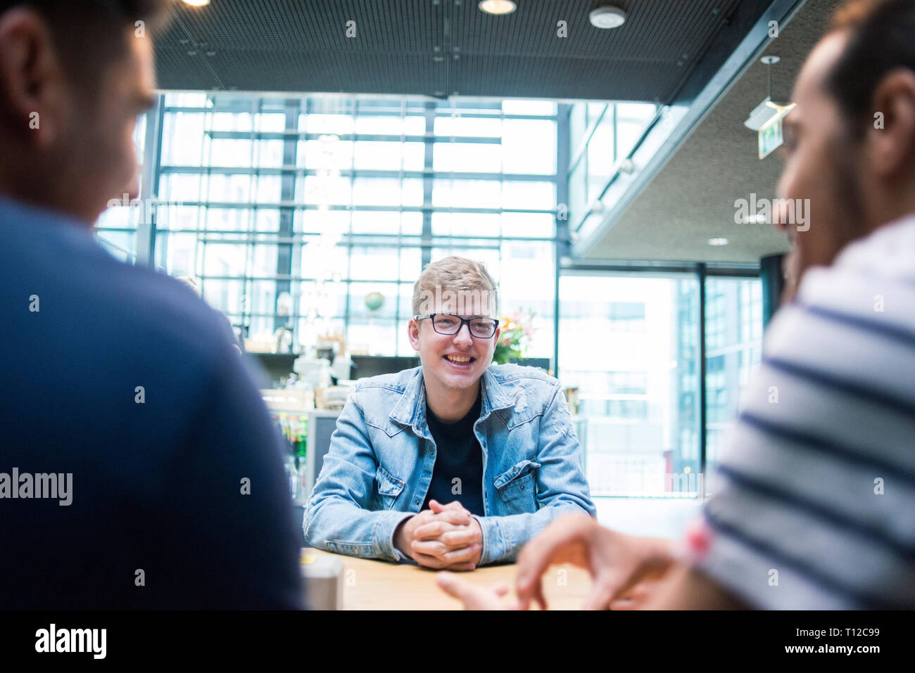 A group of young people sitting around a table chatting with each other ...