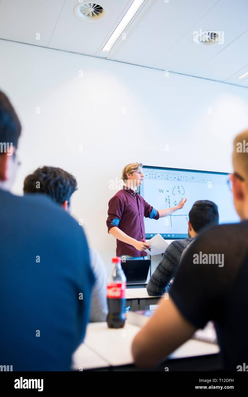 A teacher teaches a lesson in a classroom with a computer screen as a ...