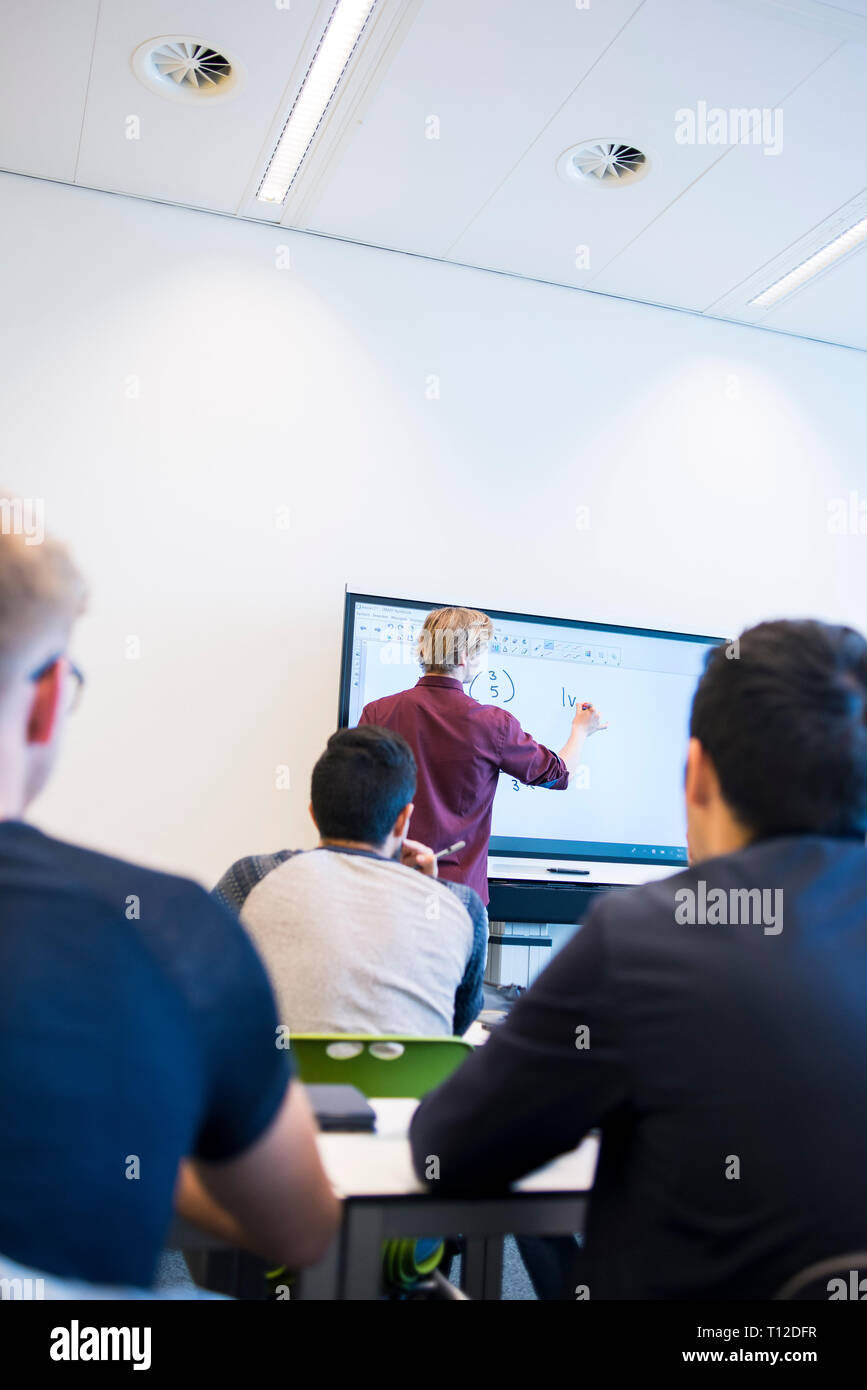 A teacher teaches a lesson in a classroom with a computer screen as a ...