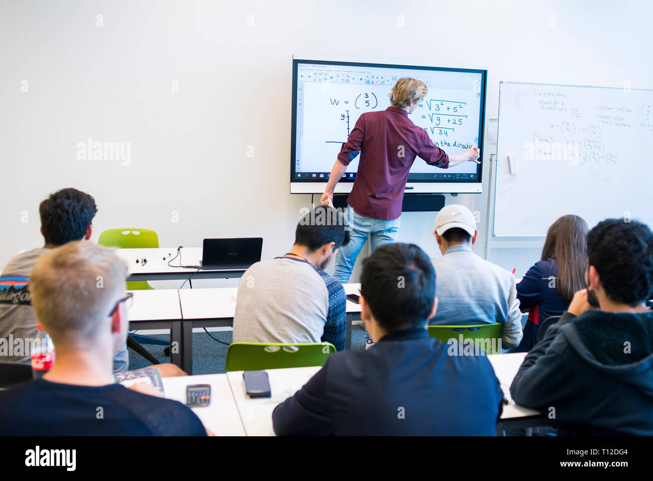 A teacher teaches a lesson in a classroom with a computer screen as a ...