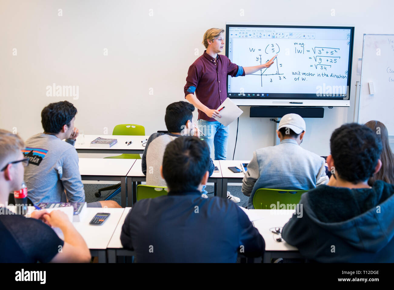 A teacher teaches a lesson in a classroom with a computer screen as a ...