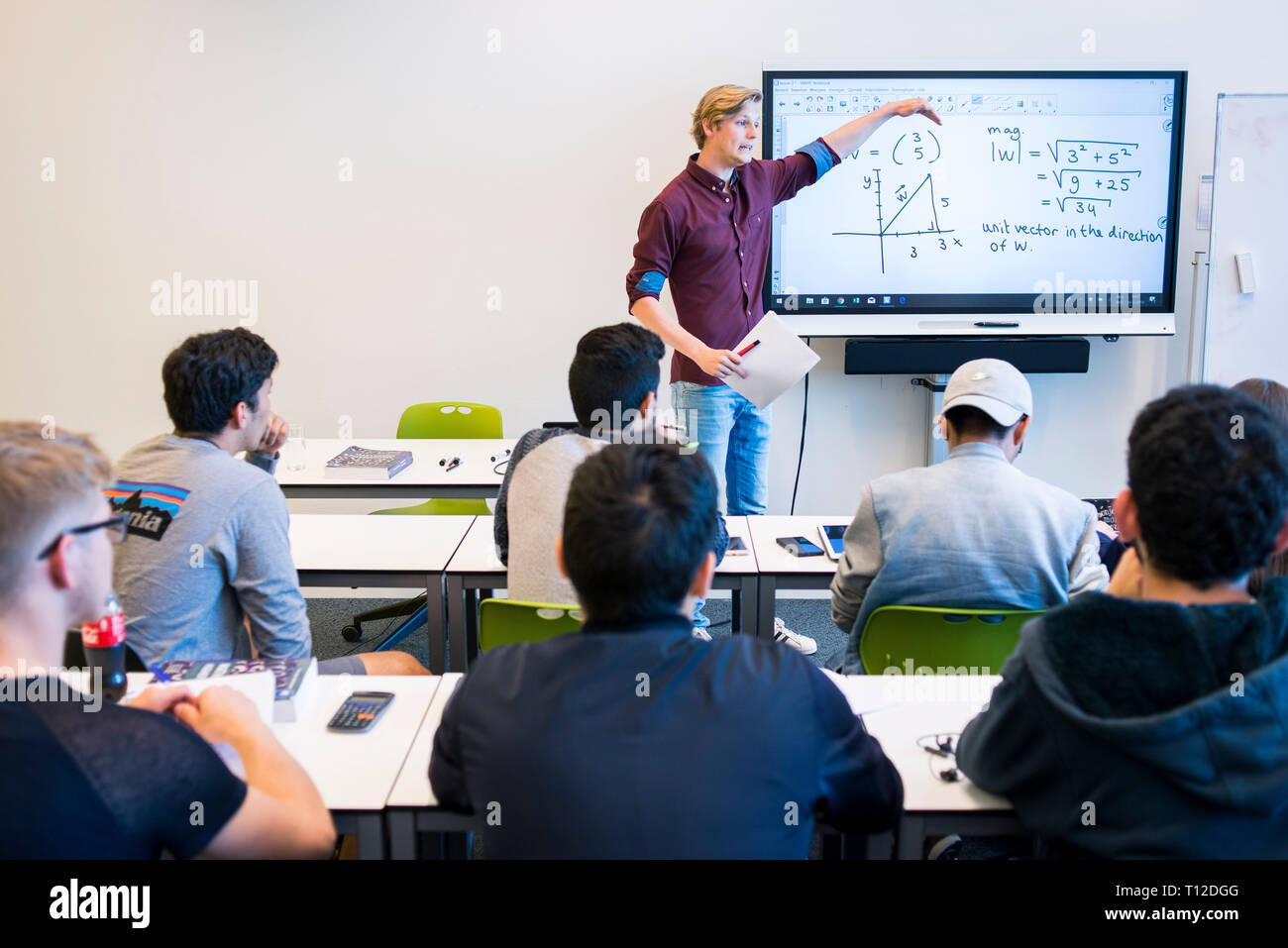 A teacher teaches a lesson in a classroom with a computer screen as a ...