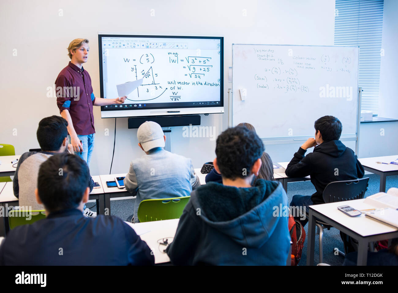A teacher teaches a lesson in a classroom with a computer screen as a ...