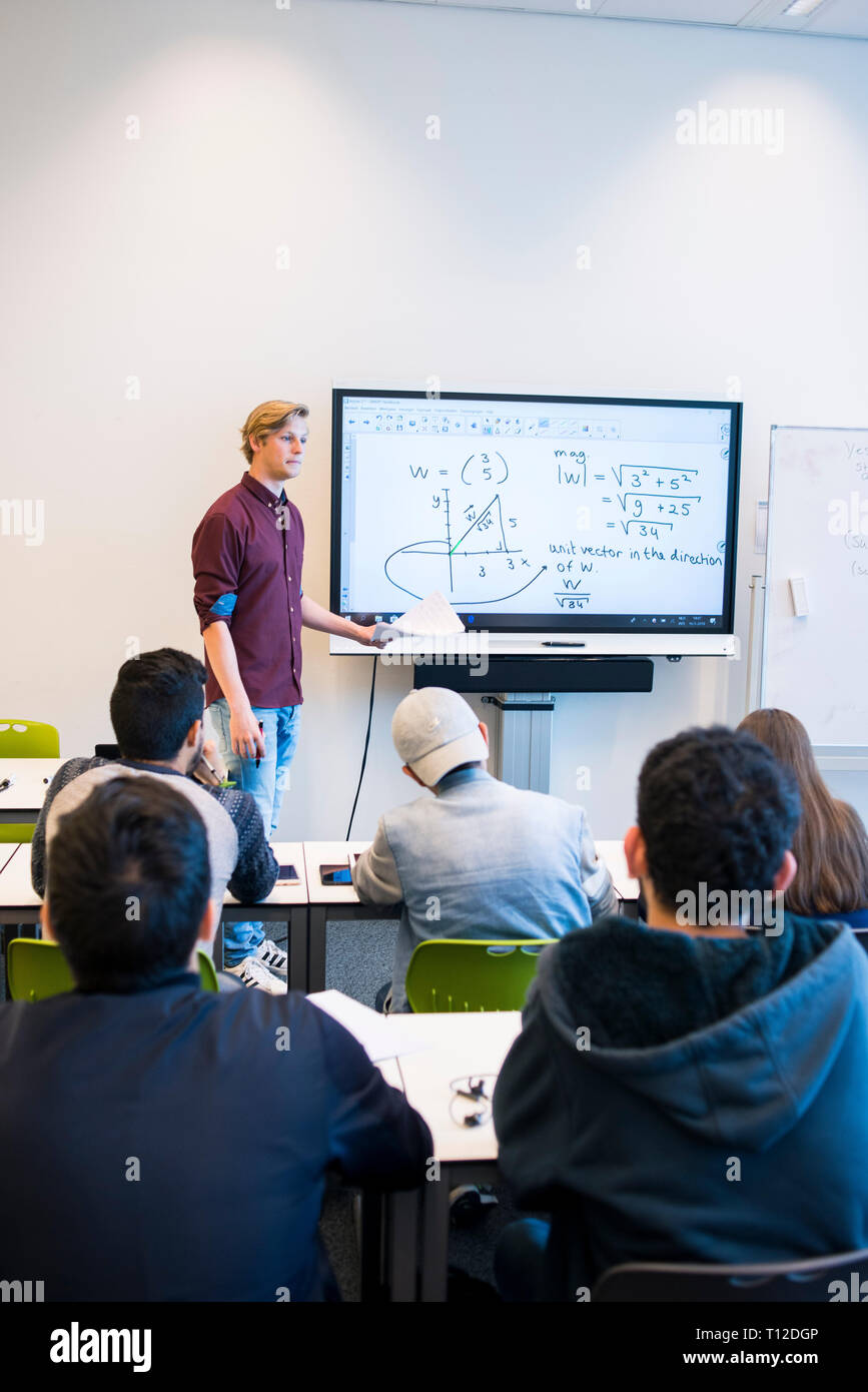 A teacher teaches a lesson in a classroom with a computer screen as a ...