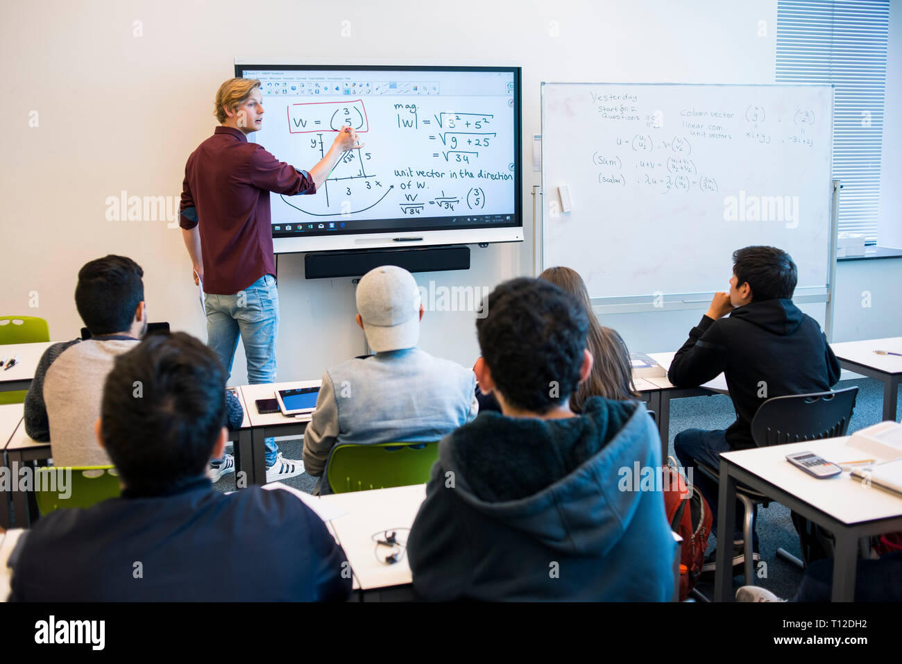 A teacher teaches a lesson in a classroom with a computer screen as a ...