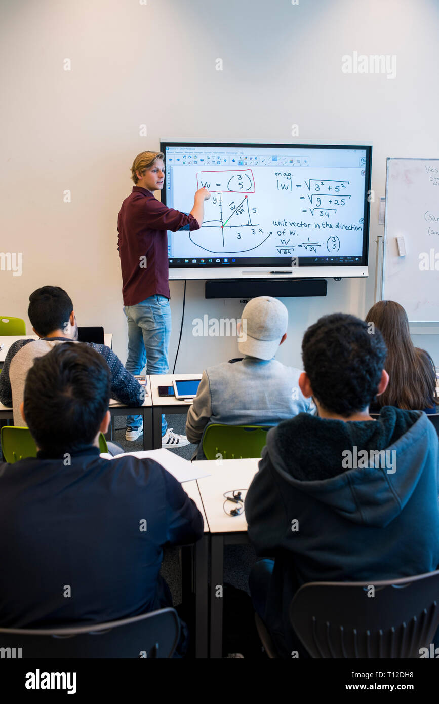 A teacher teaches a lesson in a classroom with a computer screen as a ...