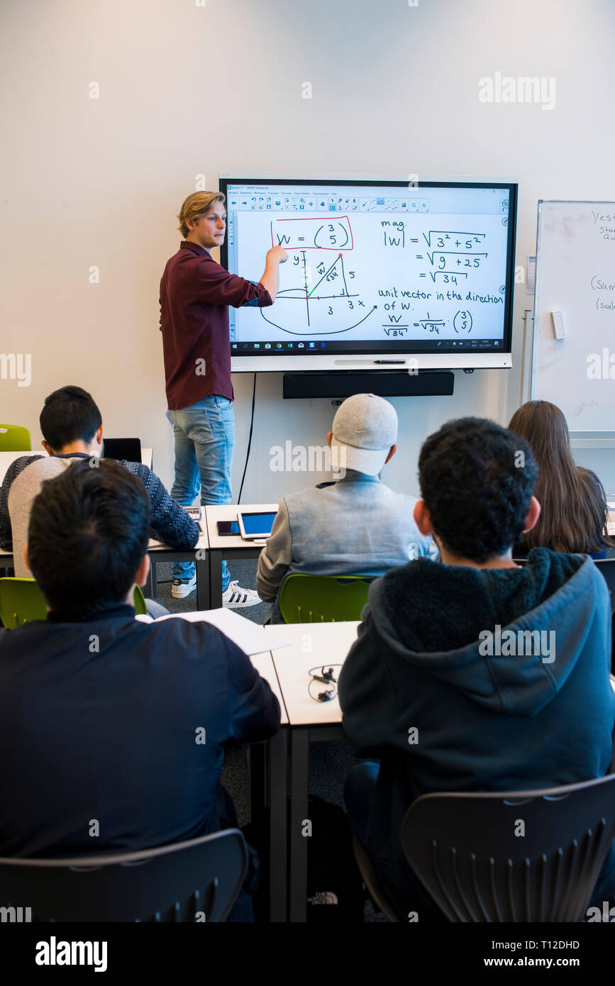 A teacher teaches a lesson in a classroom with a computer screen as a ...