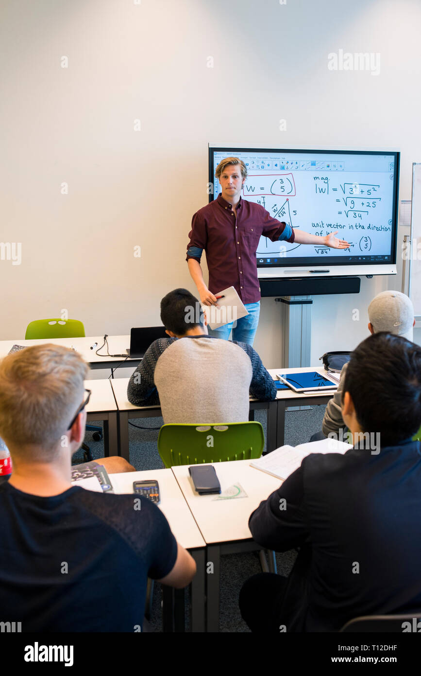 A teacher teaches a lesson in a classroom with a computer screen as a ...