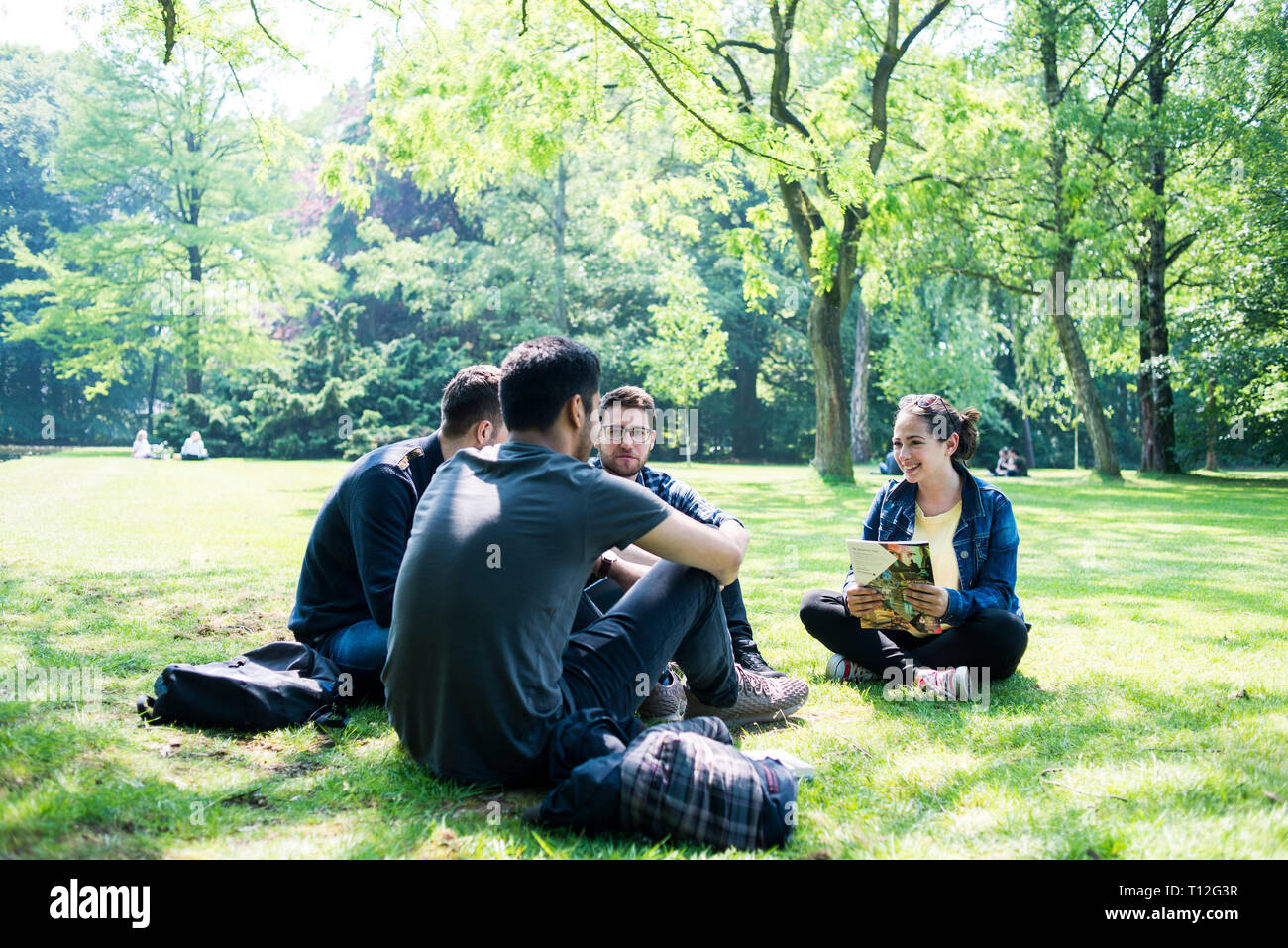 A group of young international students sit outside on college campus ...