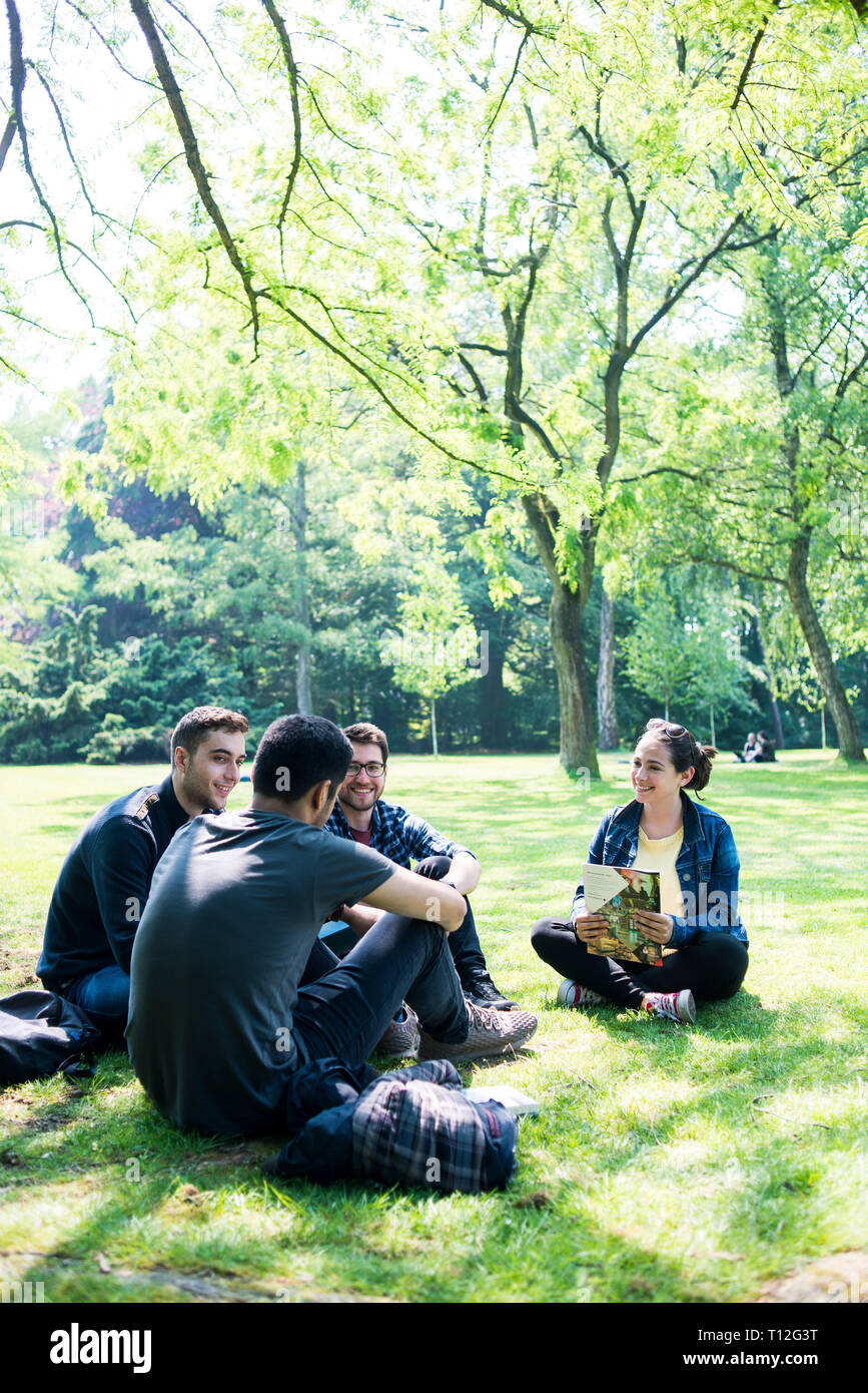 A group of young international students sit outside on college campus ...