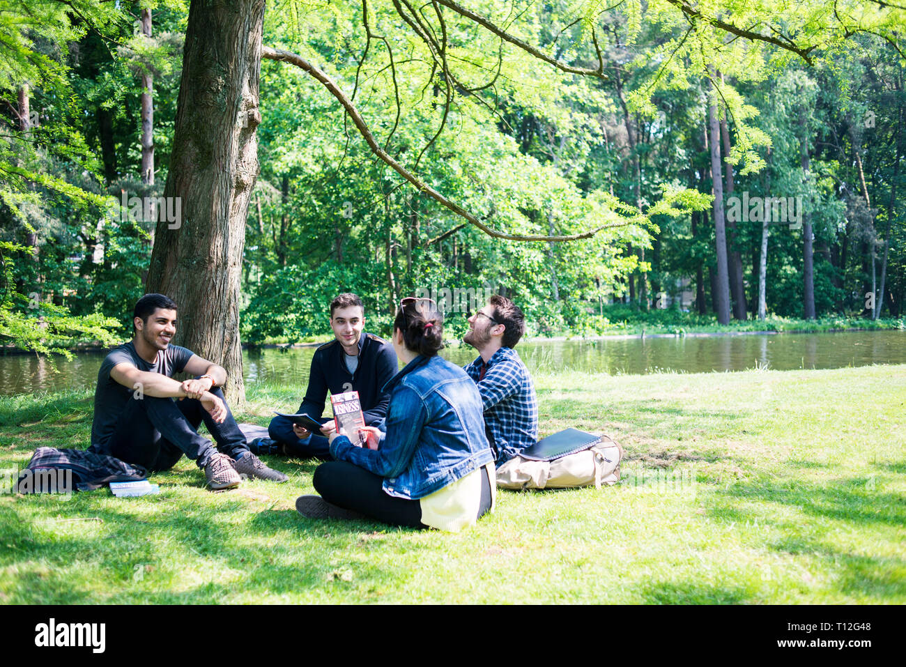 A group of young international students sit outside on college campus ...