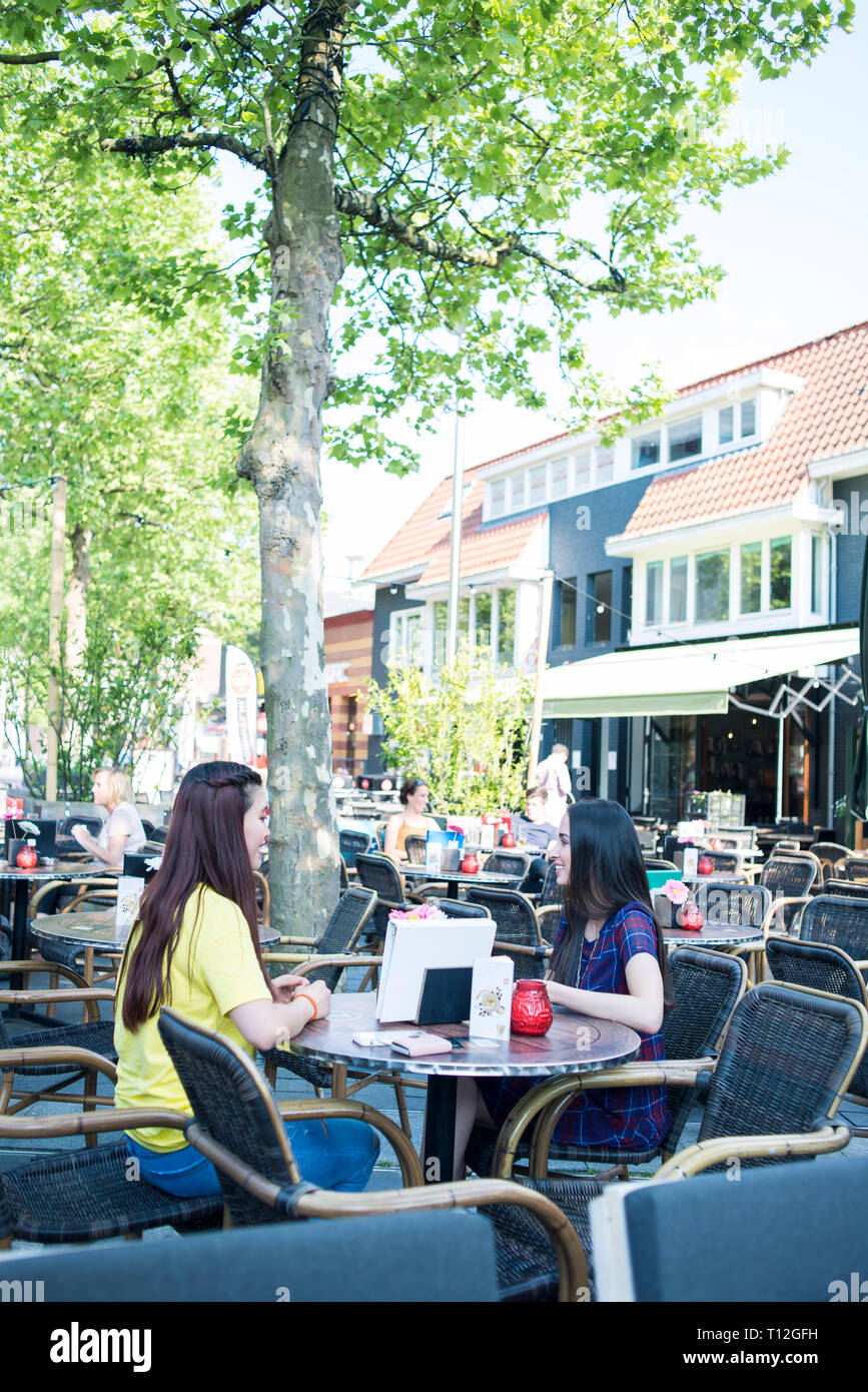 Two young international students sit outside a coffee shop / bar ...