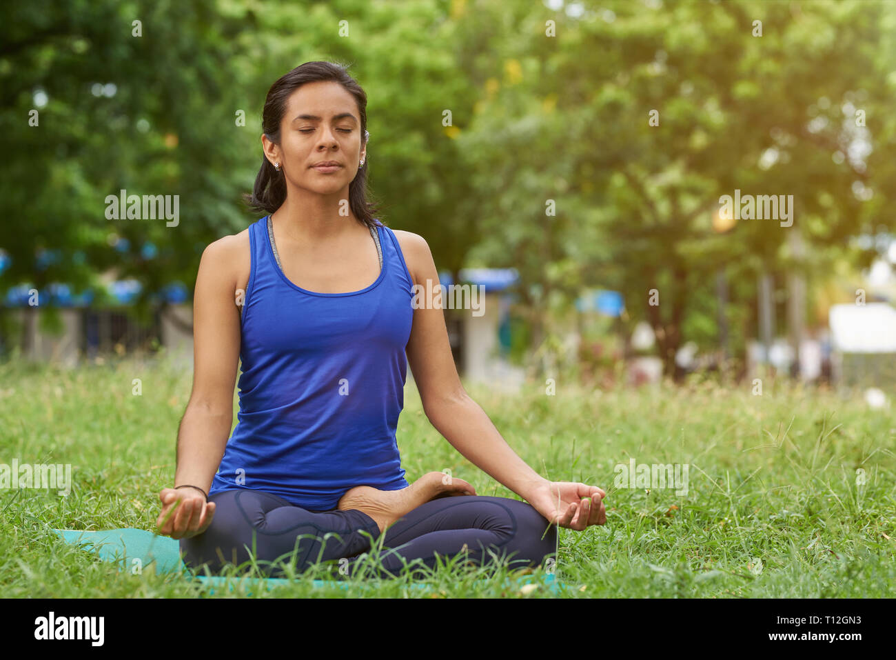 Young woman breathing in yoga pose on green natural park background ...