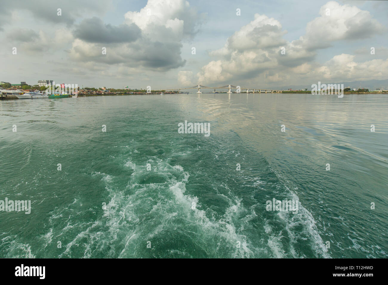 Wake water of a fast ferry speedboat with white foam, blue sky and deep ...