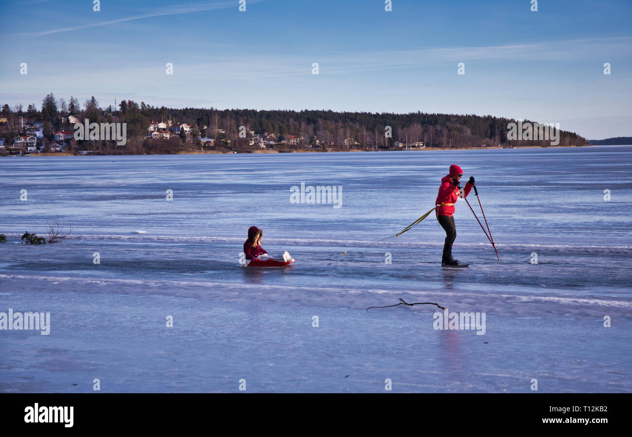 Woman ice skater with ice poles pulling a child across the ice of Lake ...