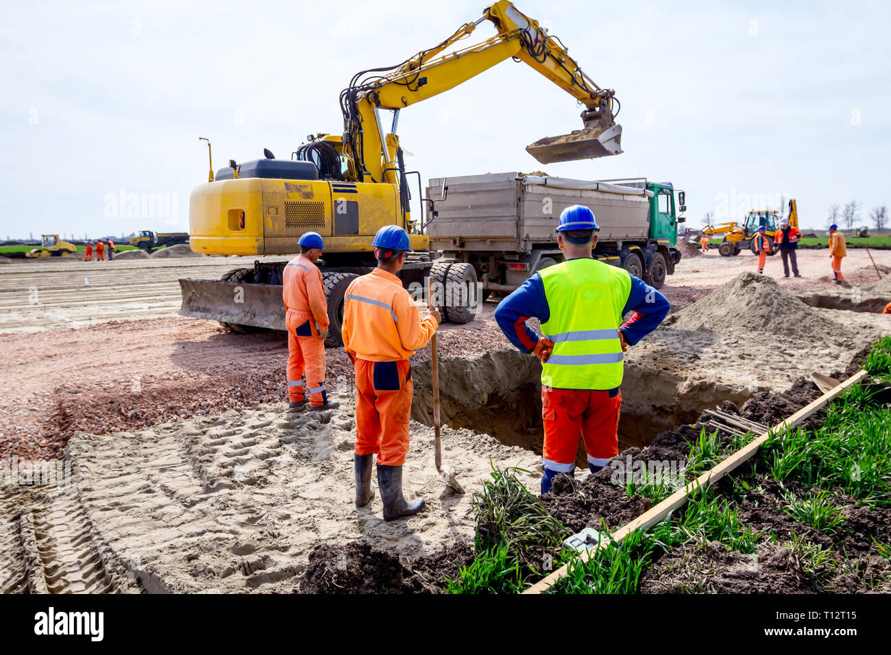 Workers are waiting for excavator to finish digging square trench on ...