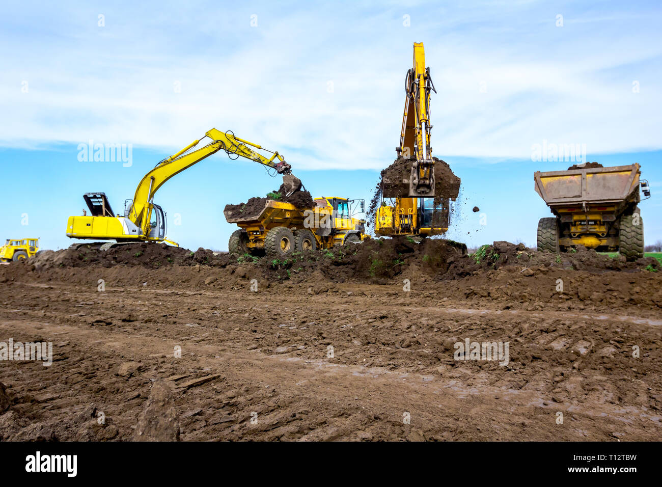 Big excavators are filling two dumper trucks with soil at construction ...