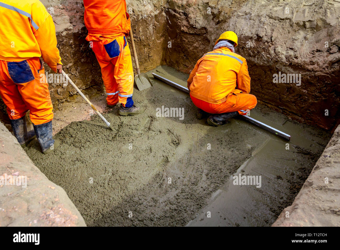 Mason is using rake to spreading fresh concrete in square trench Stock ...