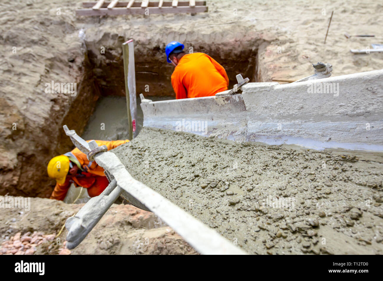 Workers are spreading fresh concrete in square trench pouring from ...
