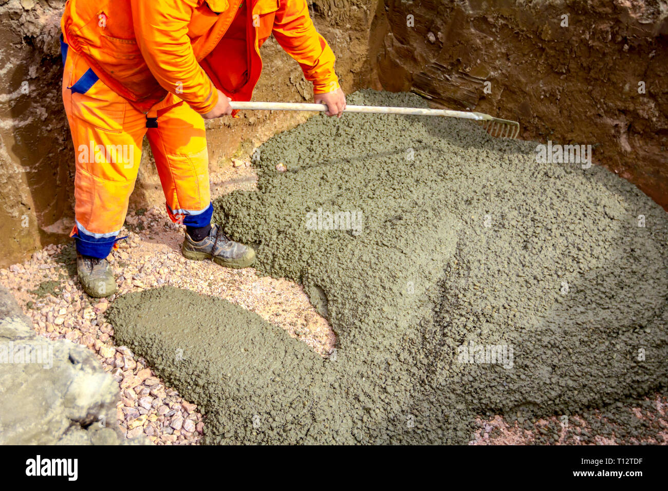 Mason is using rake to spreading fresh concrete in square trench Stock ...