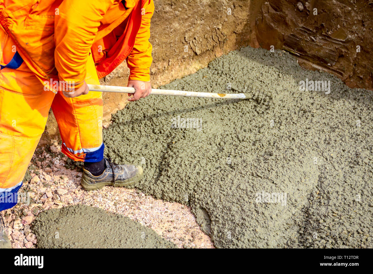 Mason is using rake to spreading fresh concrete in square trench Stock ...