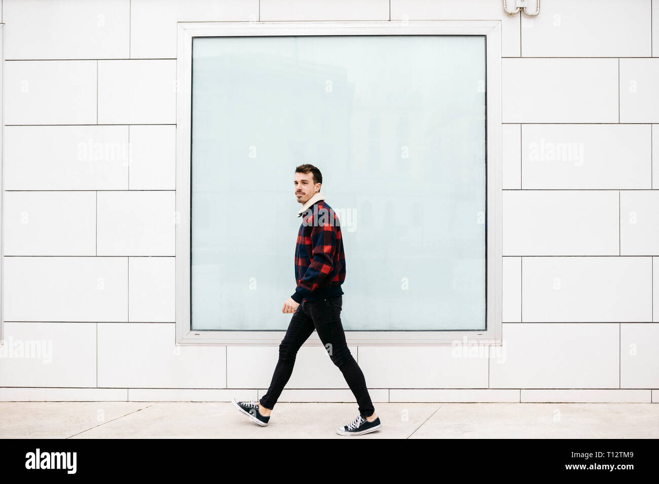 Young man with casual clothes walking with a white wall and a large ...