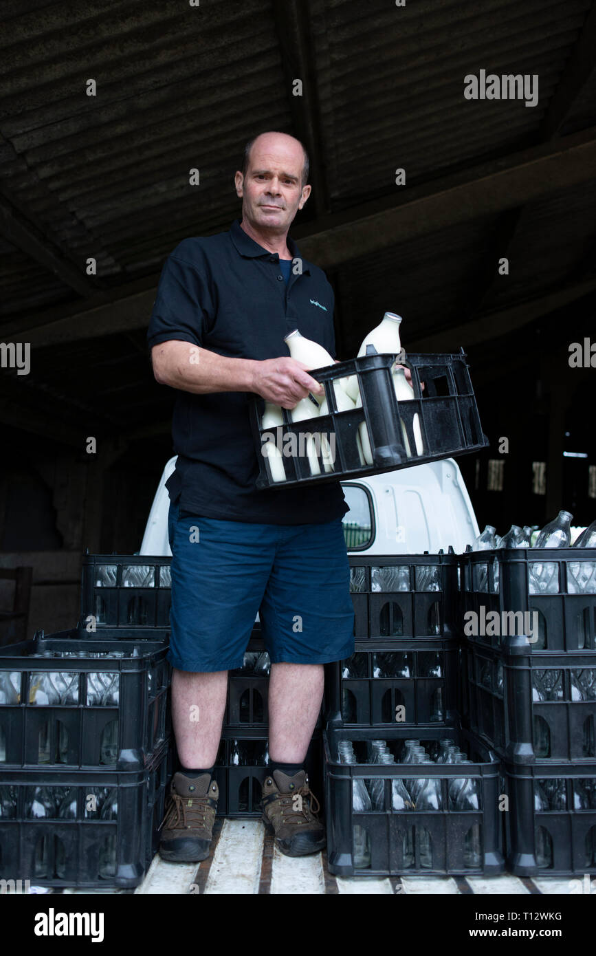 A real milk man stands on his milk float with milk bottles in a crate ...