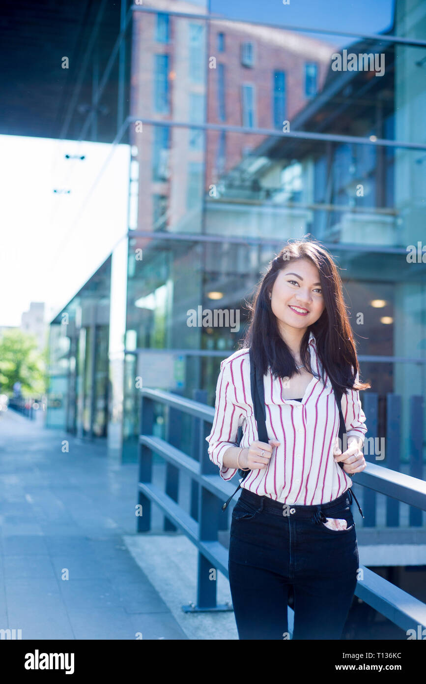 A female Asian student in a modern college campus poses for a photo ...